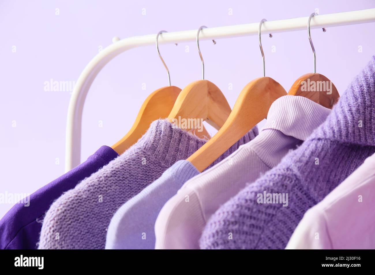 Rack with clothes in purple shades on lilac background, closeup Stock ...