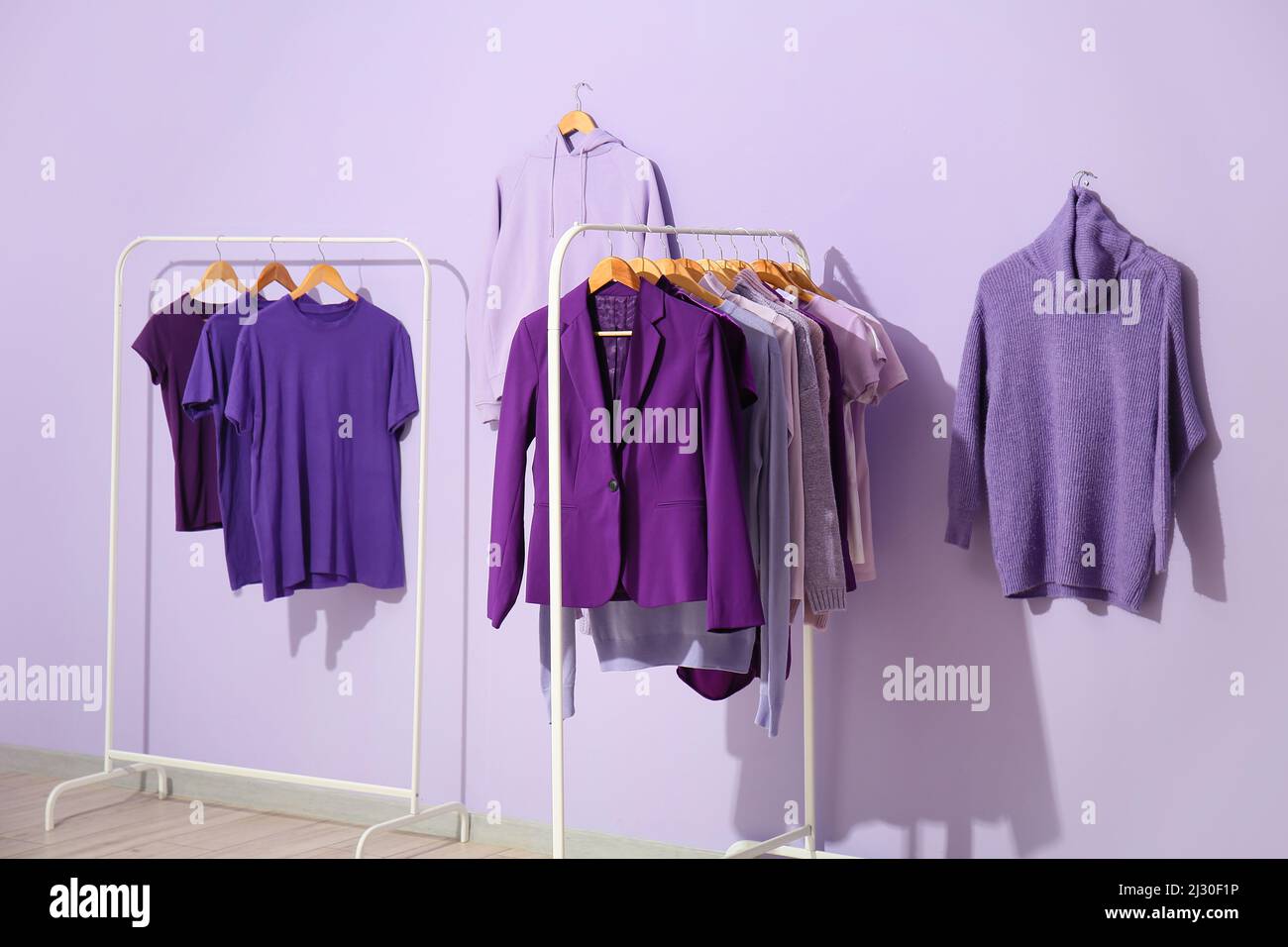 Racks with clothes in purple shades near lilac wall Stock Photo - Alamy