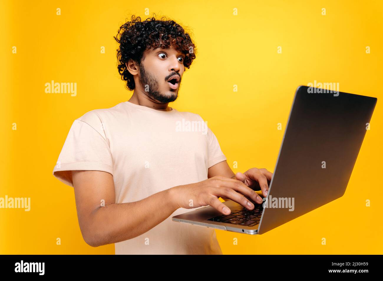 Excited Shocked Indian Or Arabian Curly Haired Guy Typing On A Laptop