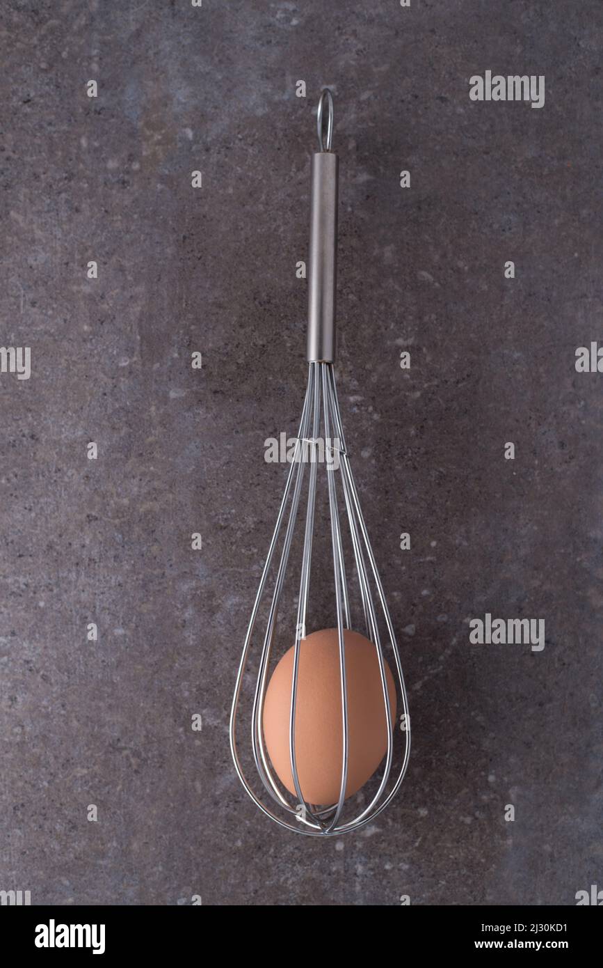 A brown chicken egg trapped in a wire whisk kitchen utensil Stock Photo ...