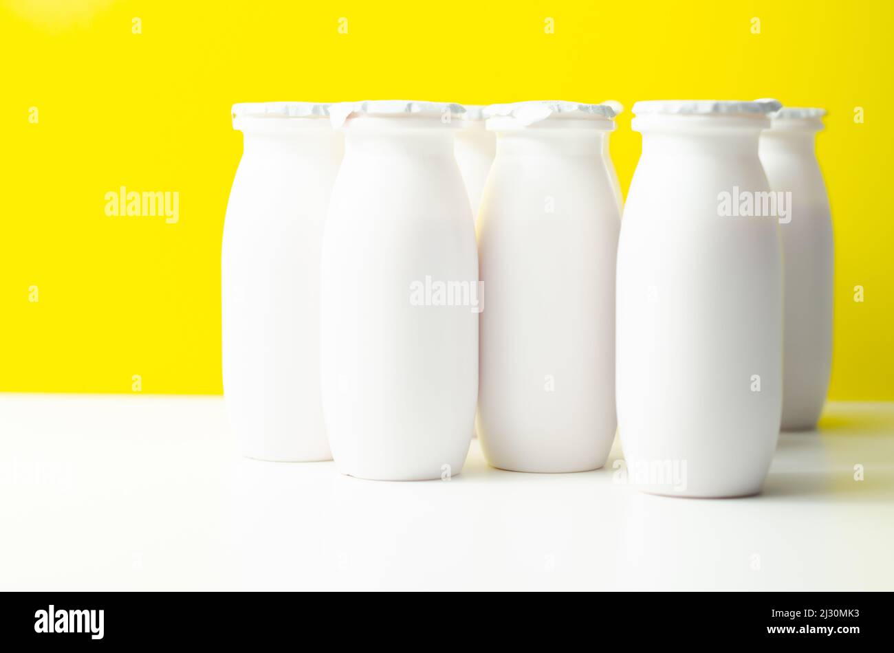 White plastic yogurt bottles on yellow background, typical packaging ...