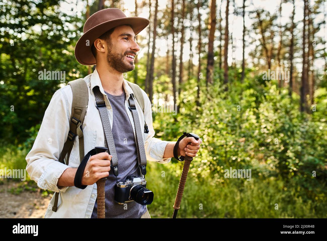Smiling young walking with hiking poles during summer trip in the woods ...