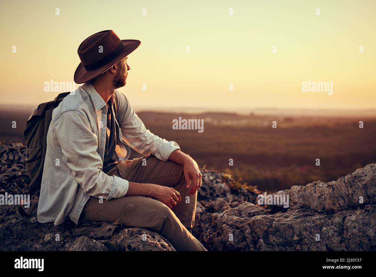 Young man enjoying sunset resting on top of mountain while hiking in ...