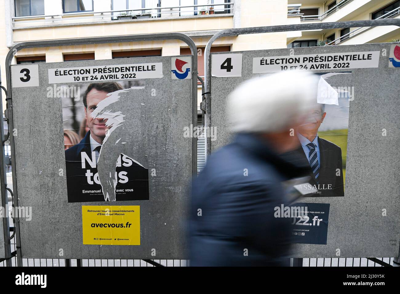 A pedestrian passes a torn official campaign poster of Emmanuel Macron ...