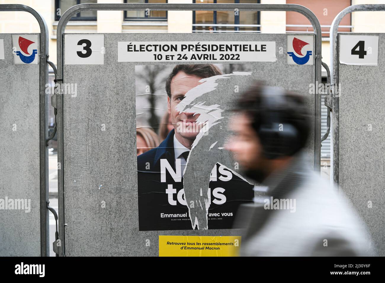 A pedestrian passes a torn official campaign poster of Emmanuel Macron ...