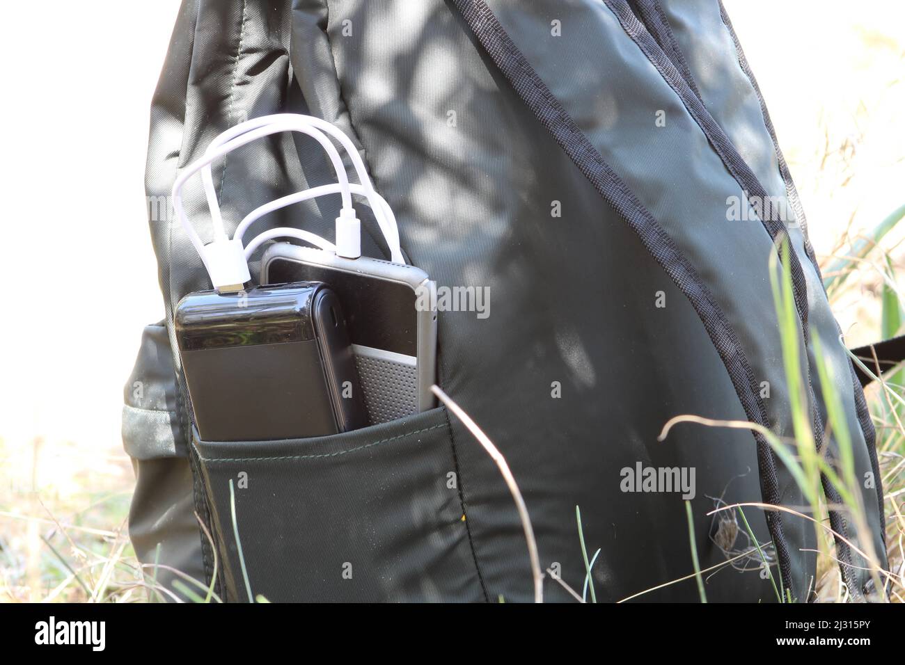 Smartphone charged with black power bank in green backpack. Close up ...