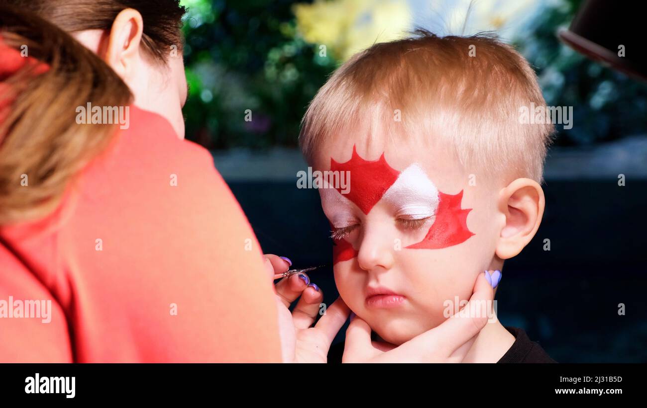 A little boy is put face painting on his face, his face is painted with ...
