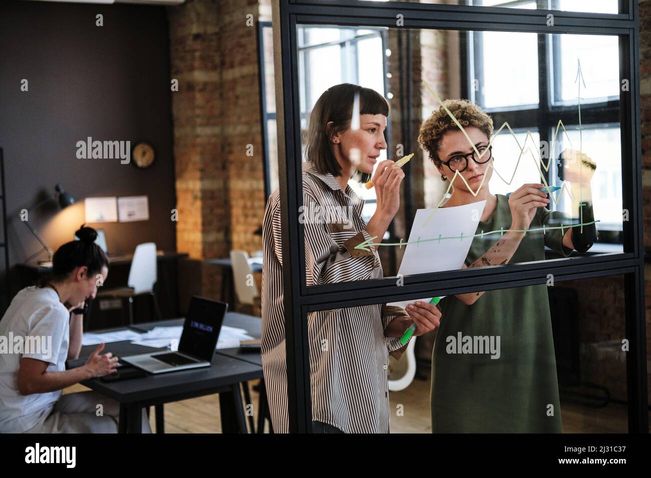 Two colleagues drawing business graphs together on glass wall and ...