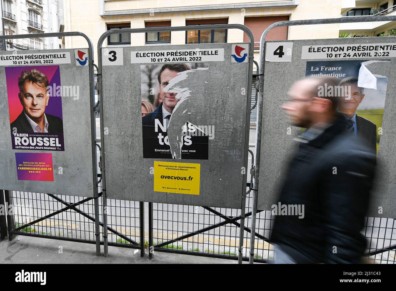 A pedestrian passes a torn official campaign poster of Emmanuel Macron ...