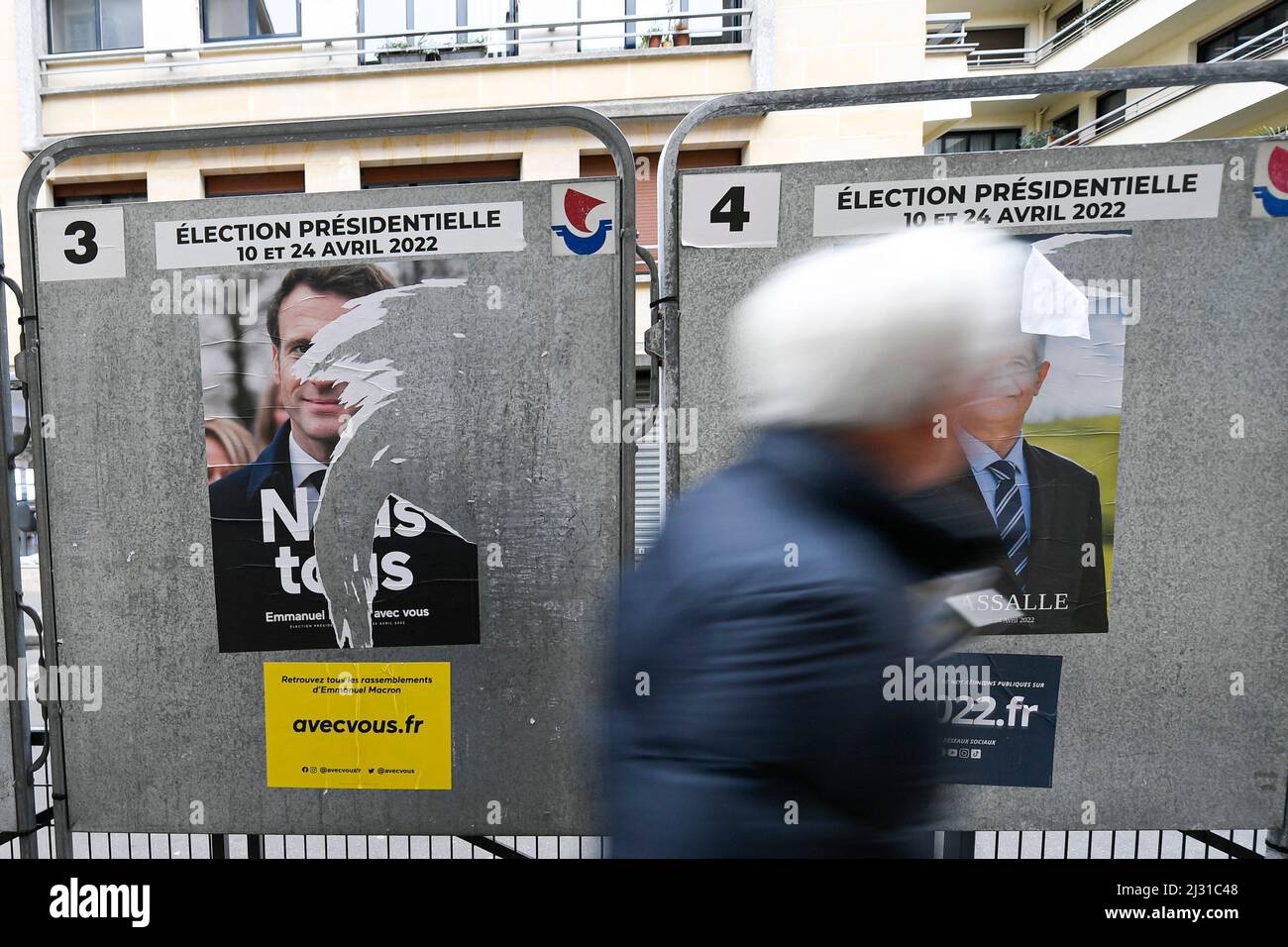 A pedestrian passes a torn official campaign poster of Emmanuel Macron ...