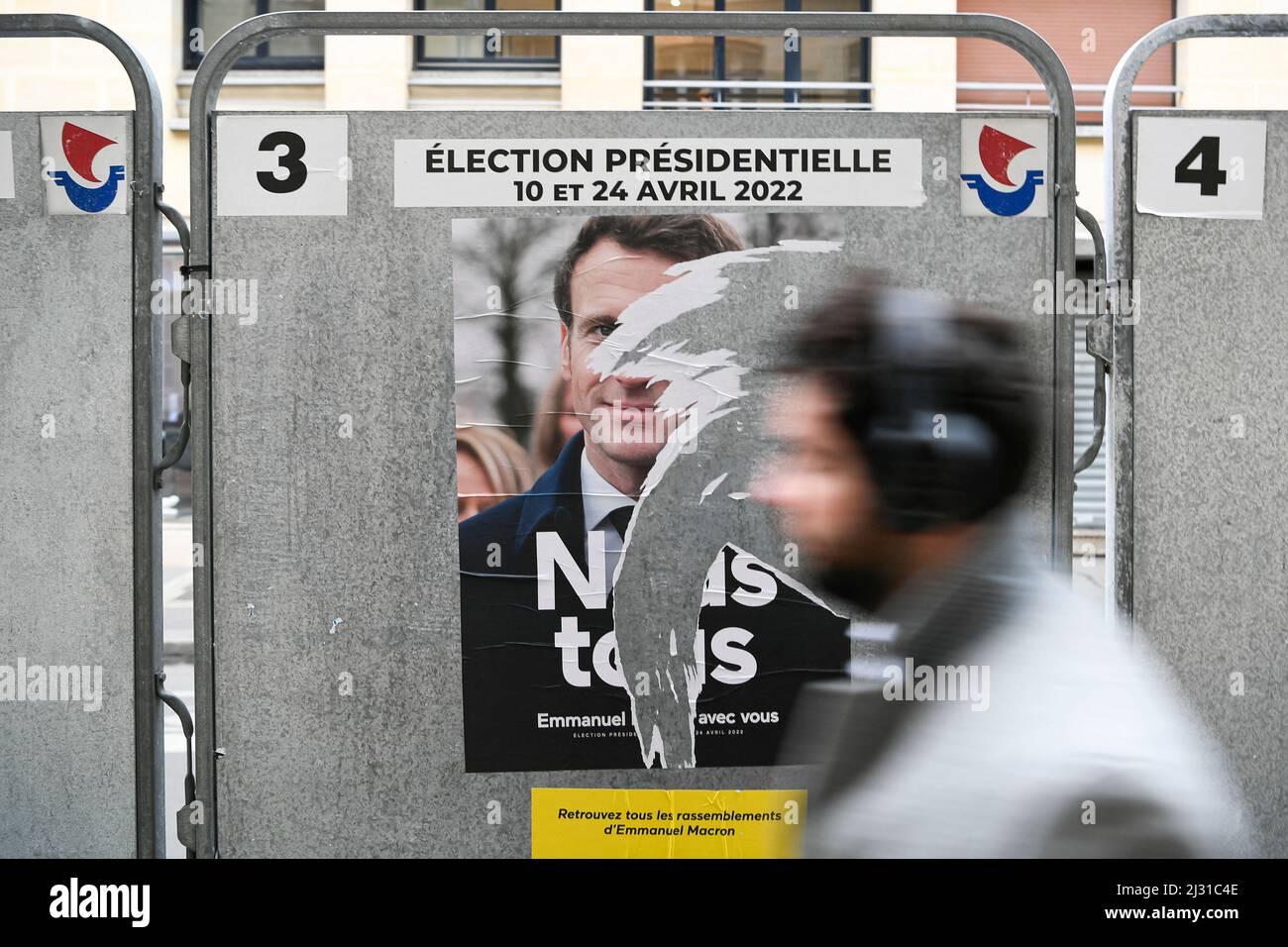 A pedestrian passes a torn official campaign poster of Emmanuel Macron ...