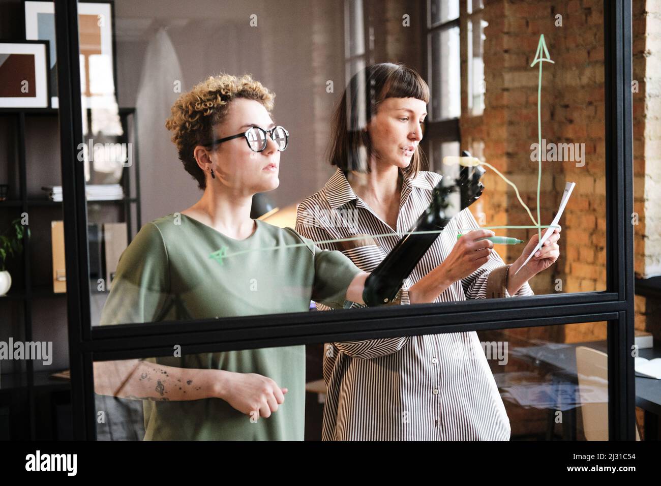 Young woman with prosthetic arm drawing graphs on glass wall with her ...