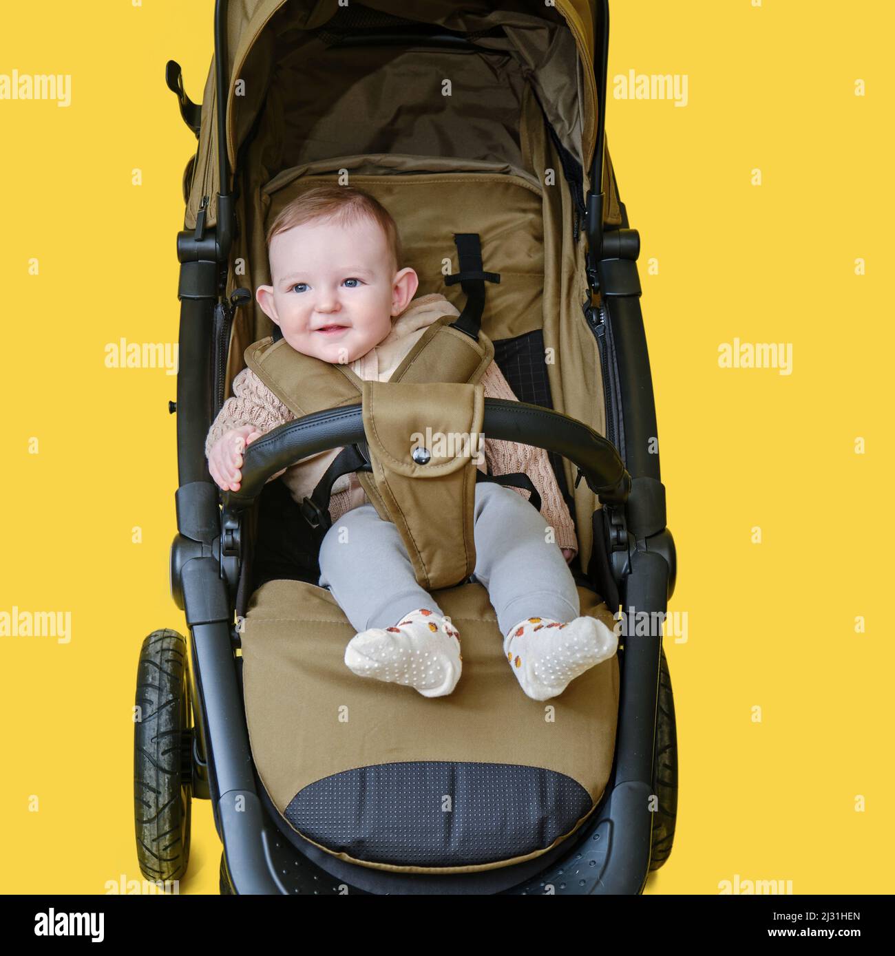 A happy child is sitting in a baby carriage on a studio yellow ...