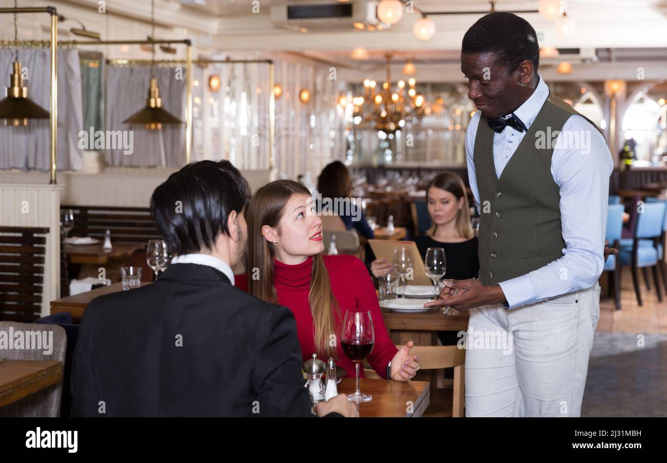 Positive couple talking with African American waiter Stock Photo - Alamy