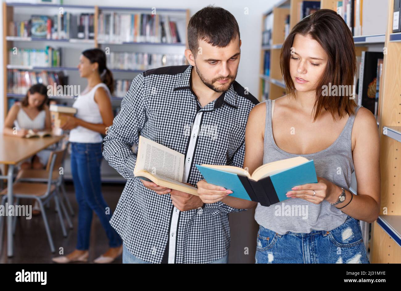 Young students studying in library, reading books near bookshelves ...