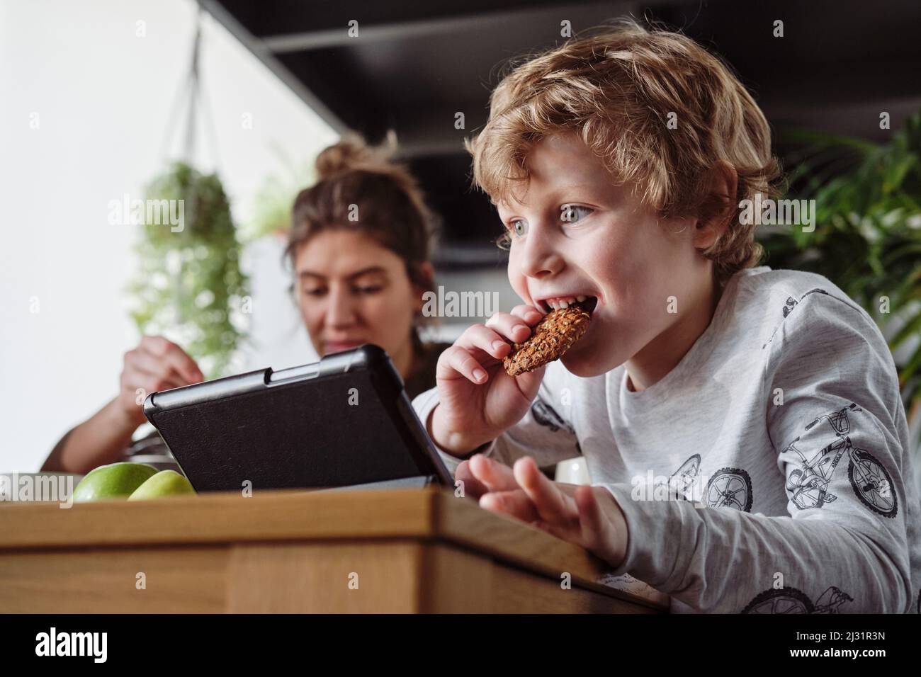 Cute child eating cookies and watching funny video on digital tablet at ...