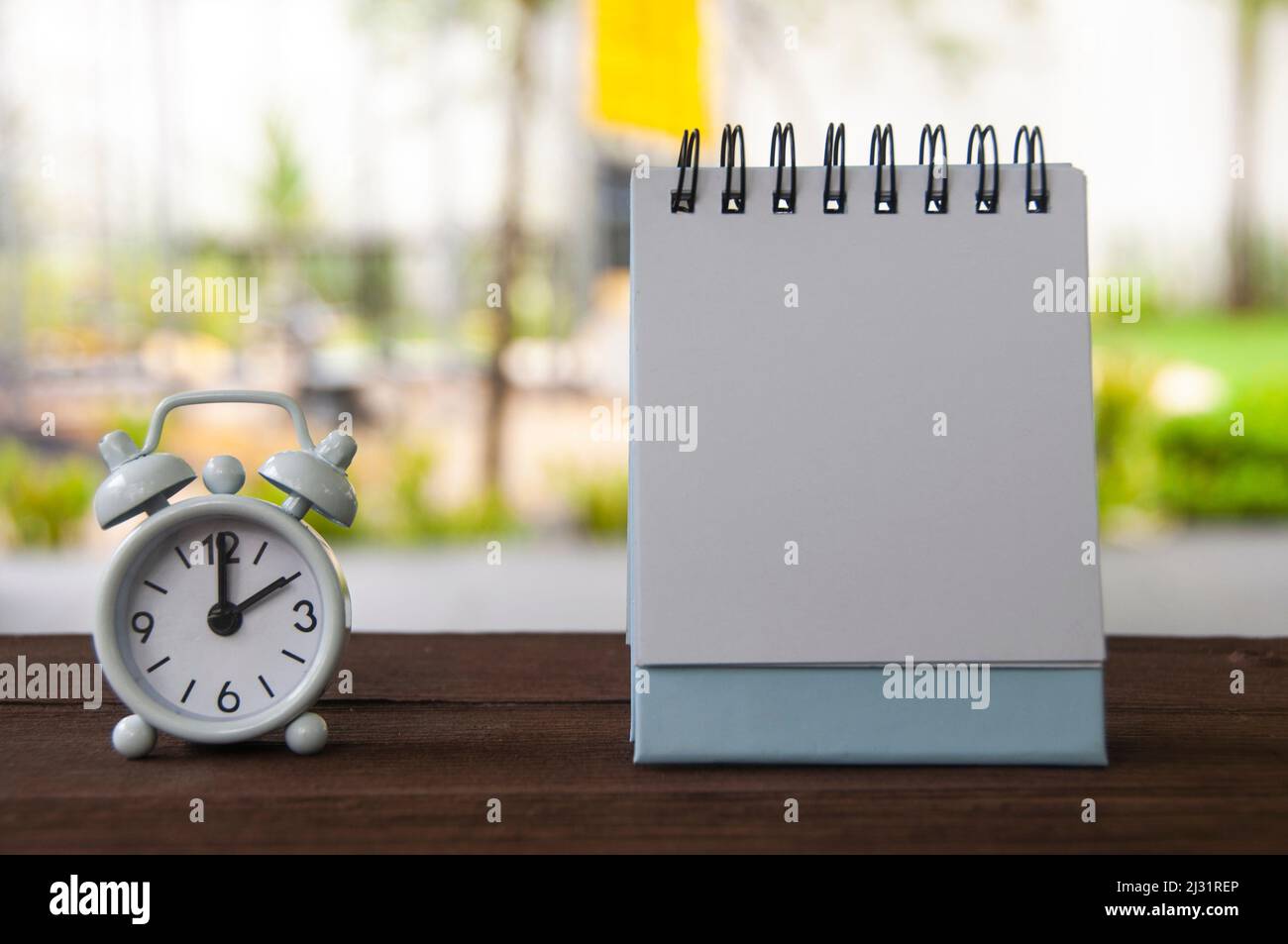 Alarm clock pointing at 2 o'clock with blank notepad on a bench. Copy ...