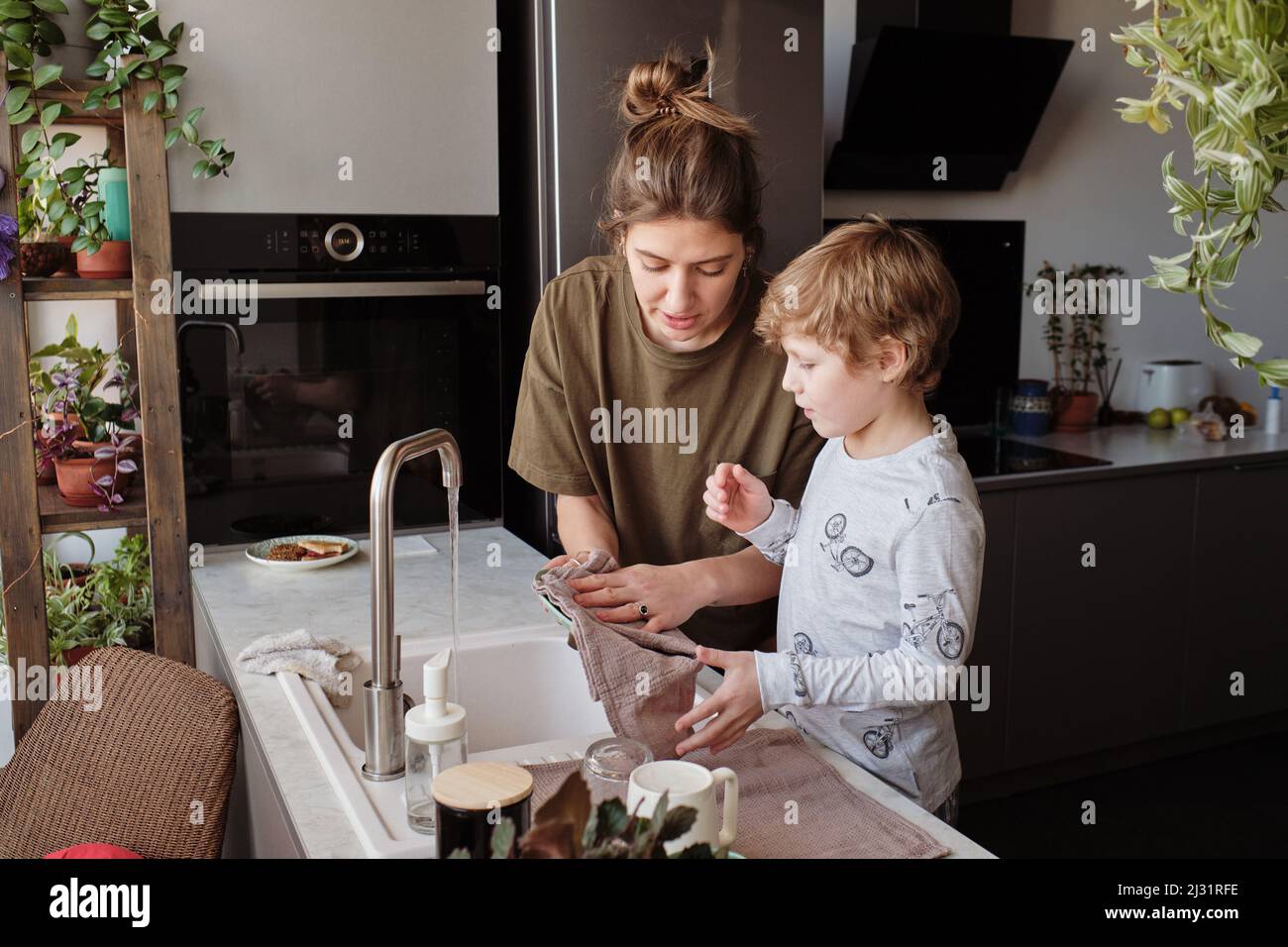 Young mother showing to her son how to wipe plates after washing, they ...