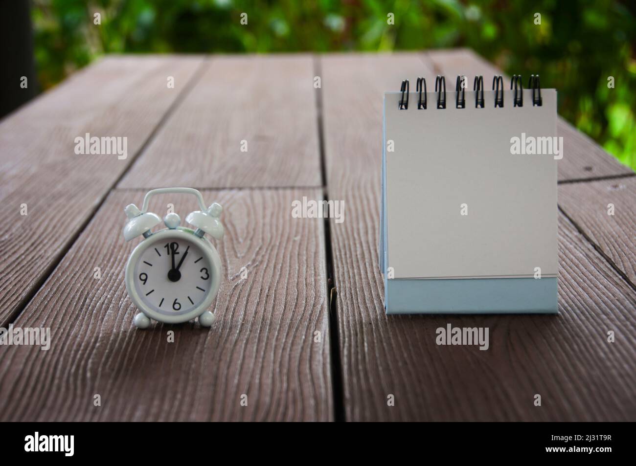 Alarm clock pointing at 1 o'clock with blank notepad on a bench. Copy ...