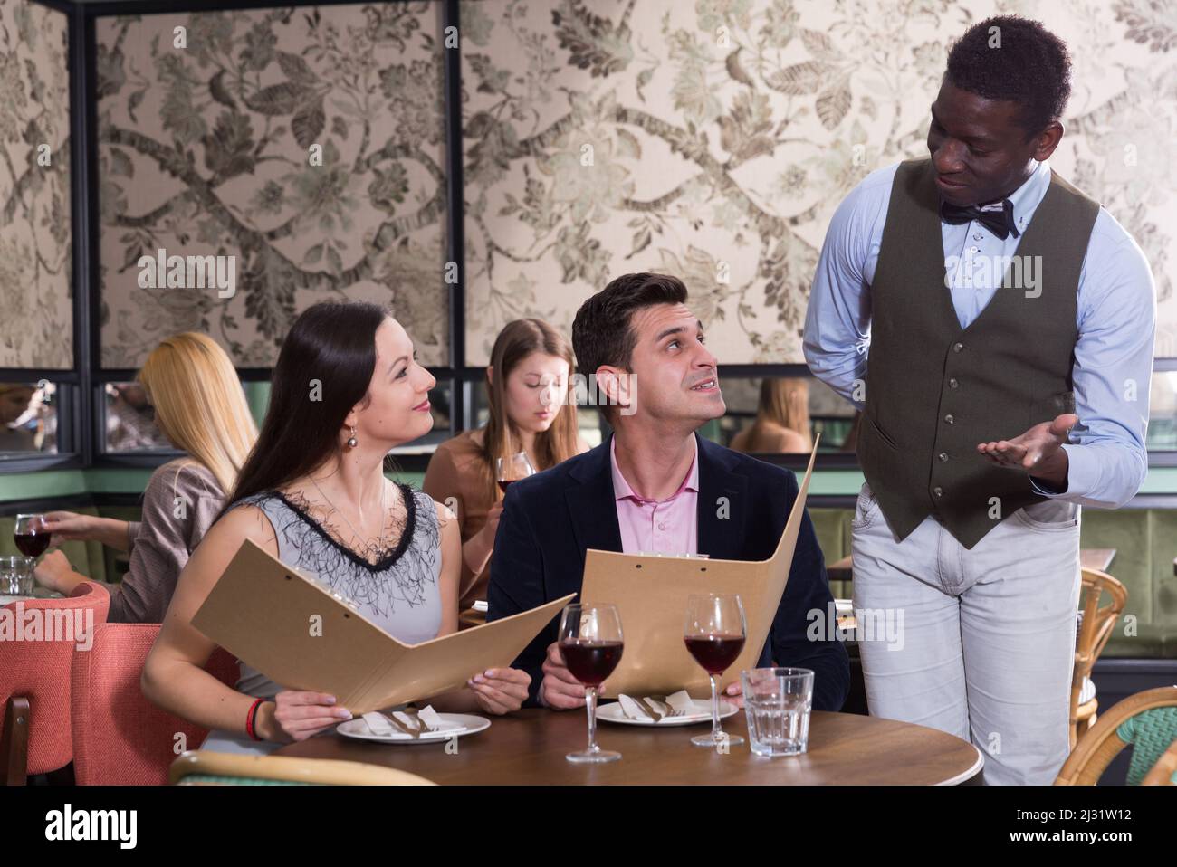 African American waiter recommending dishes from restaurant menu Stock ...