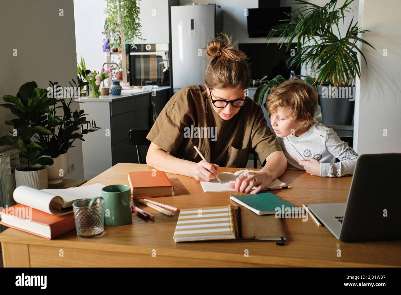 Young mother showing how to write to her son while they doing homework ...