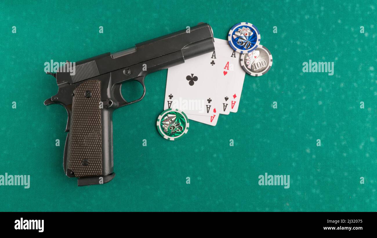 A top shot of a weapon next to some playing cards and dice on a poker ...