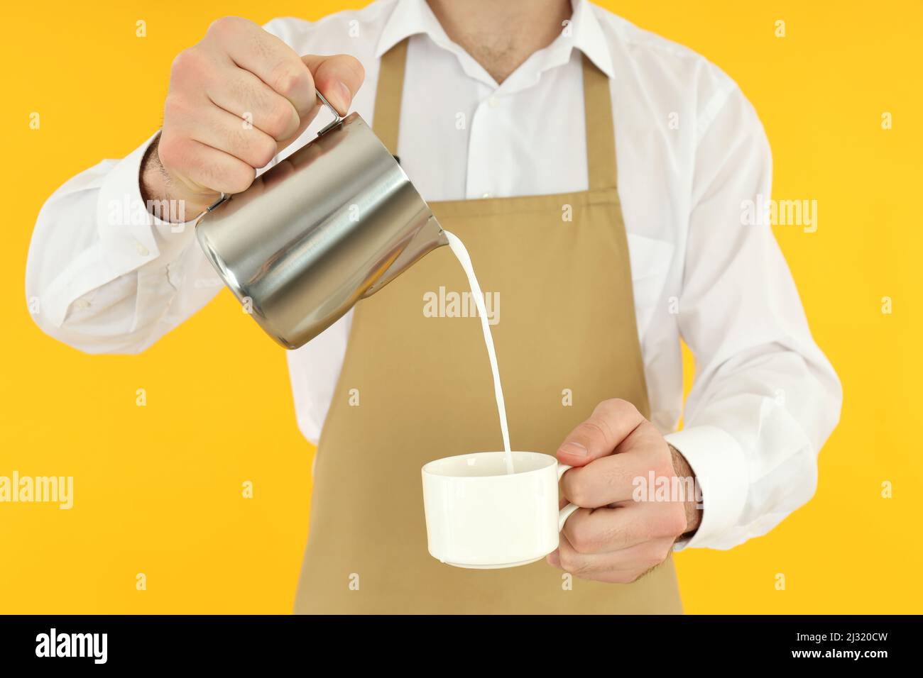 Waiter man pour milk on yellow background Stock Photo - Alamy