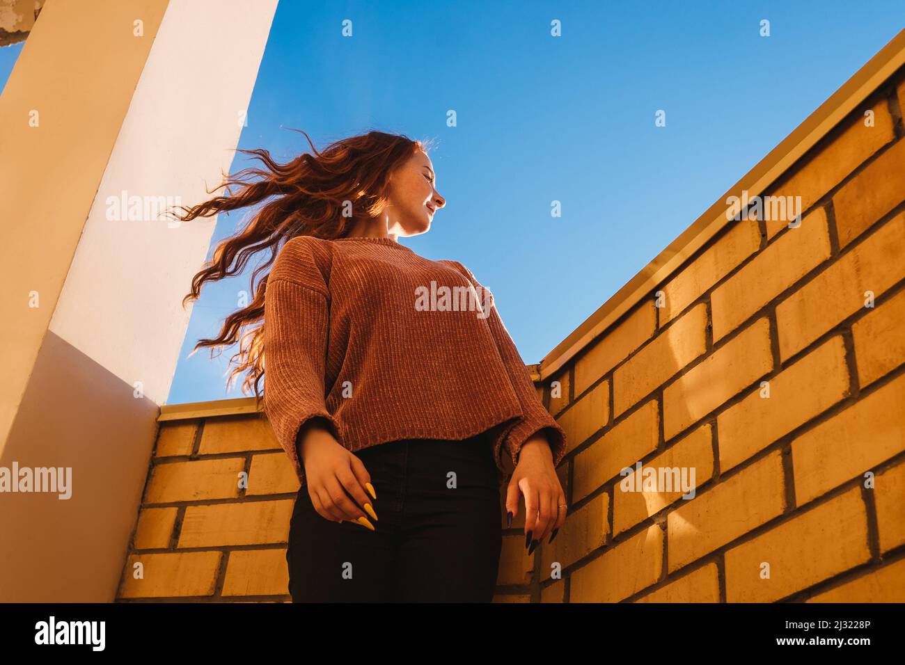 Young happy woman with long curly hair in sunshine and sky background ...