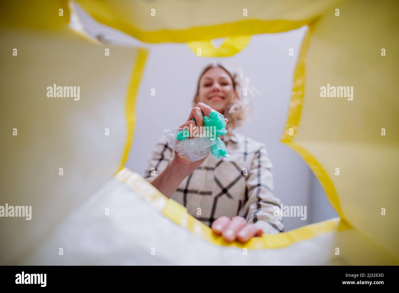 Image from inside yellow recycling bag of woman throwing a plastics to ...