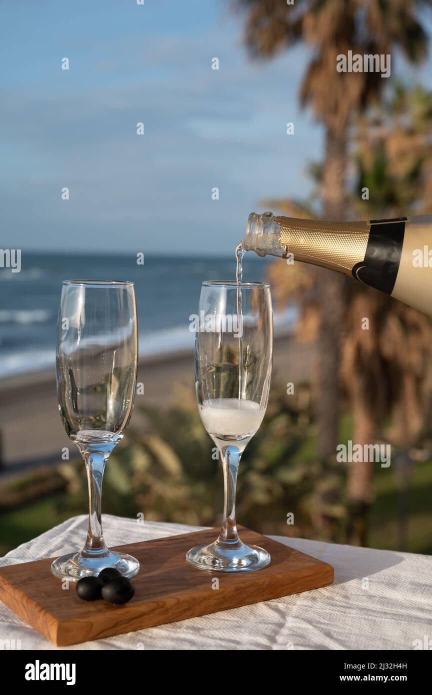 Pouring of Spanish cava sparkling wine is glasses with view on blue sea ...