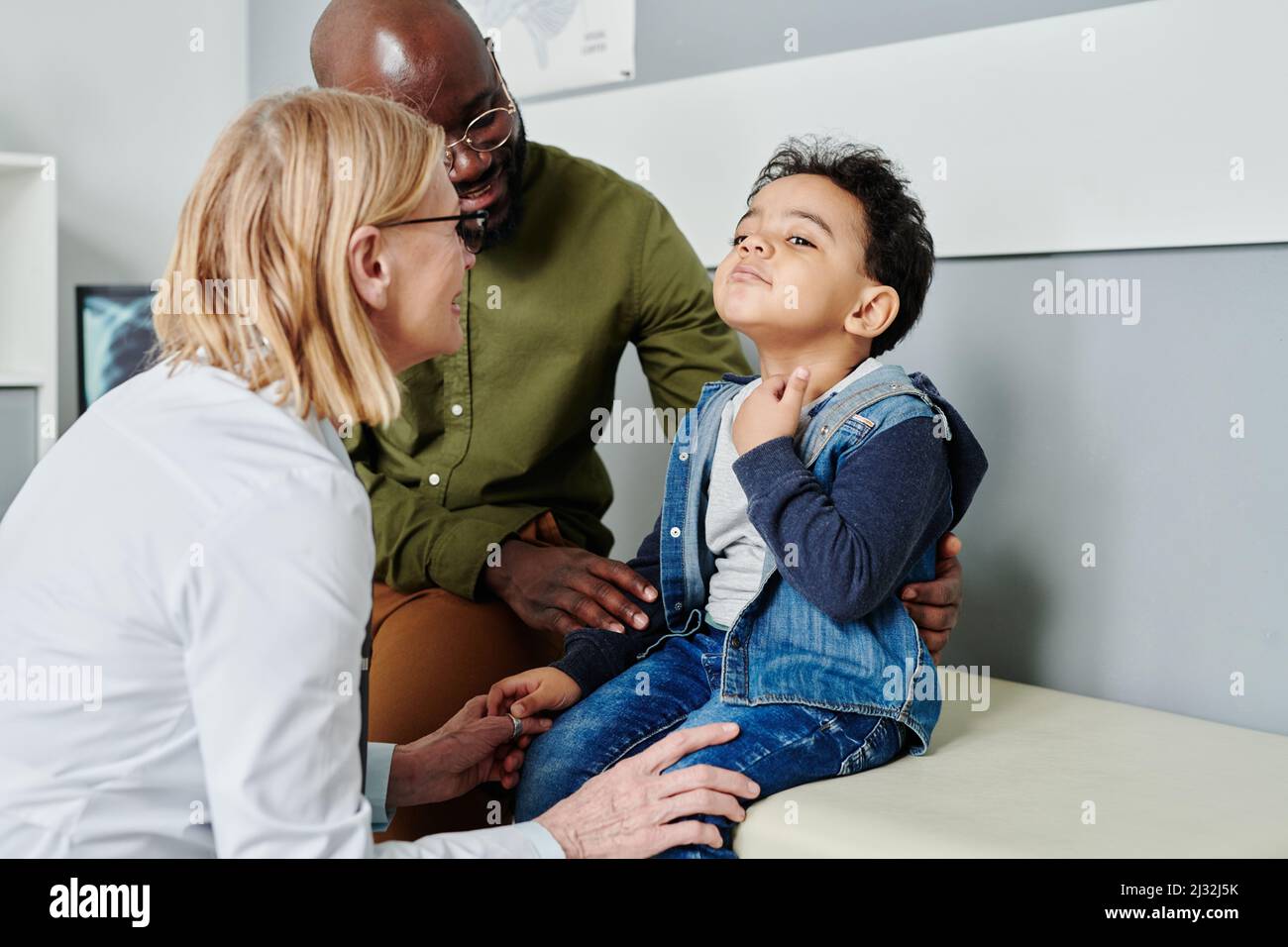 Sick little boy complaining on sore throat to mature female peditrician ...