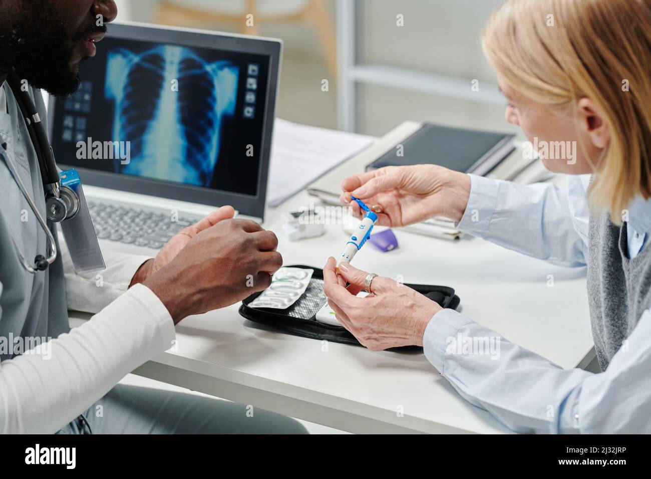 Mature female patient showing glucometer over open medical kit while ...