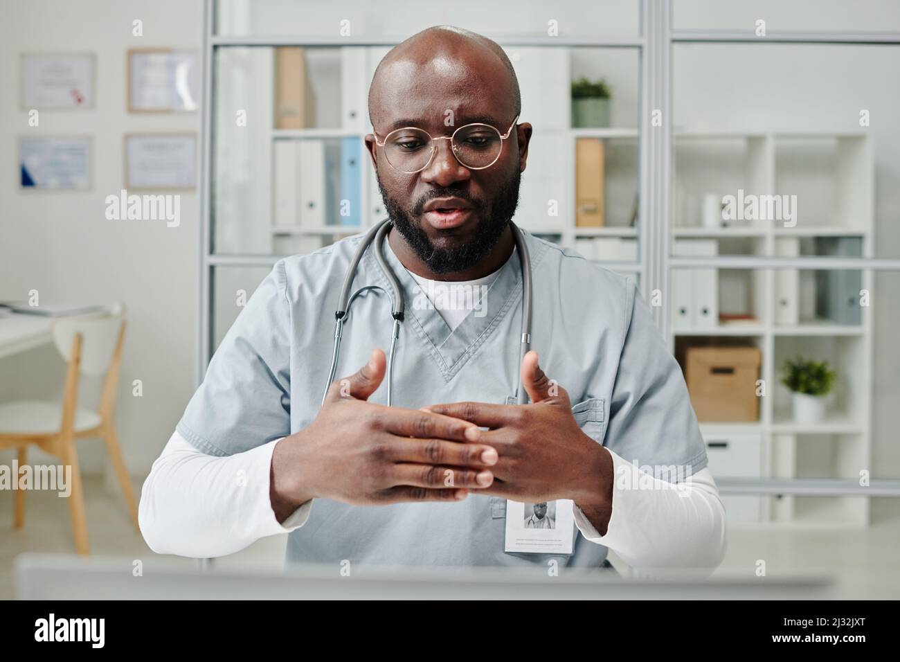 Young confident physician in eyeglasses and uniform consulting online ...