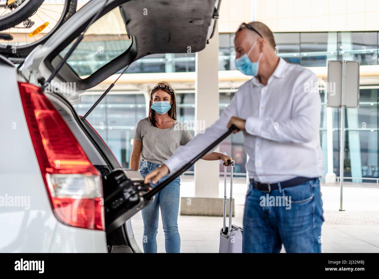 A taxi or Uber driver helping a passenger in a protective mask with her ...