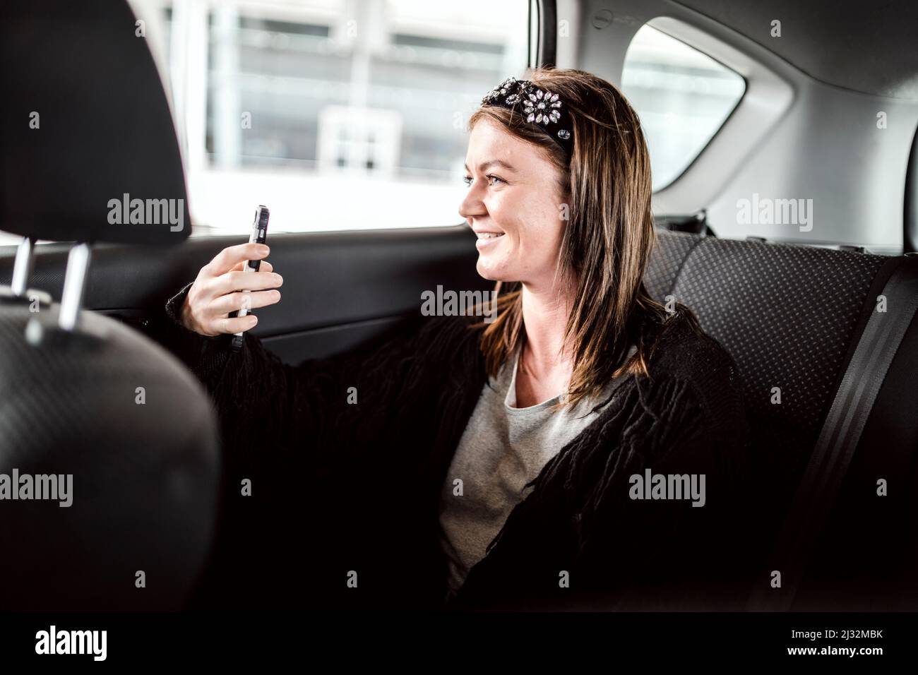 A taxi or Uber passenger talking through the phone on the car back seat ...