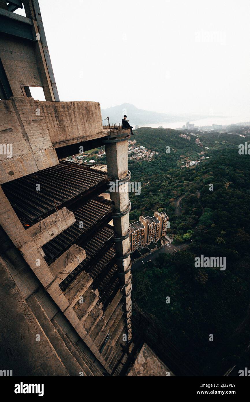A vertical shot of the man sitting on the edge of an old tall building ...