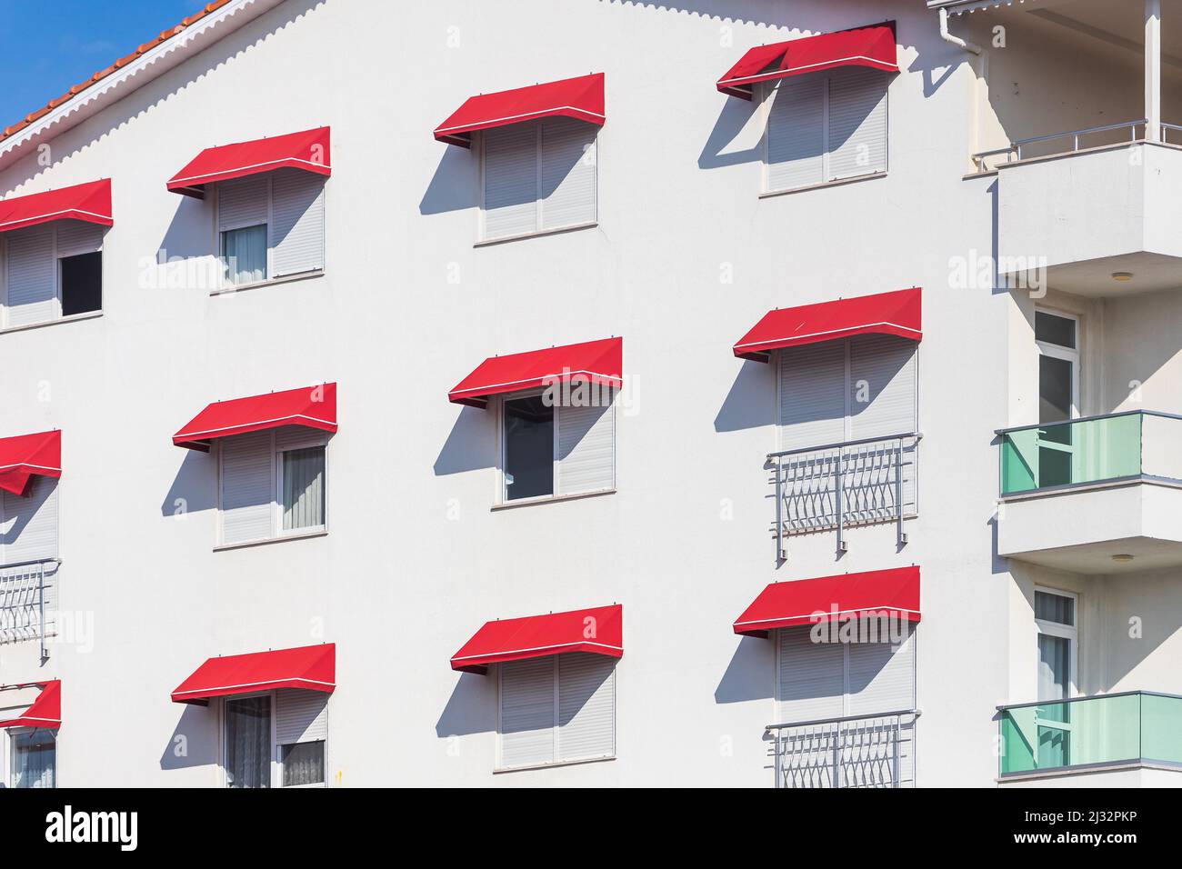 A white residential building with identical windows with a red visor ...