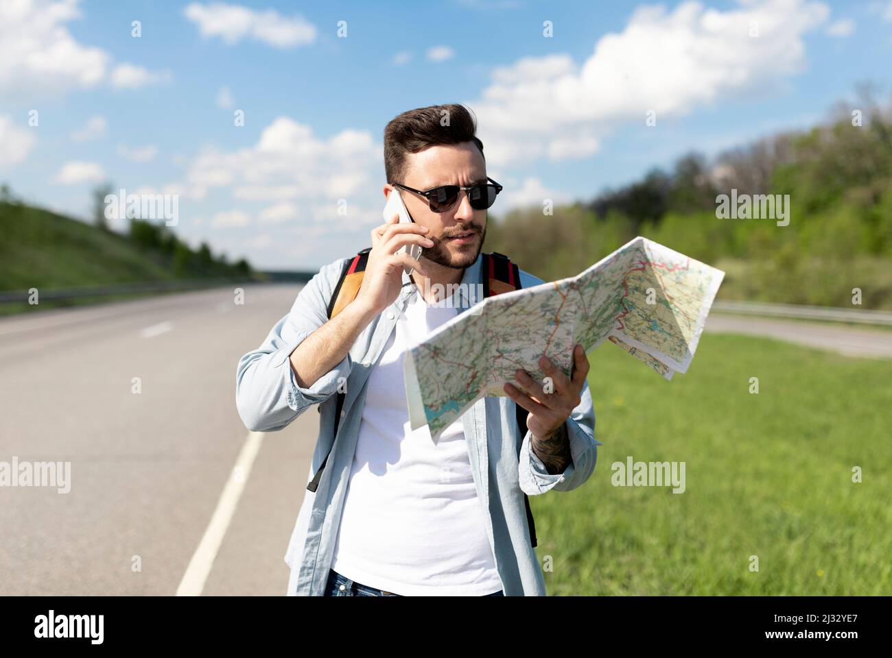 Stressed male tourist with map standing on roadside, speaking on mobile ...