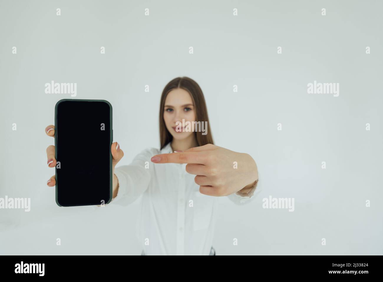 Cheerful cute woman pointing finger on smartphone screen isolated on a ...