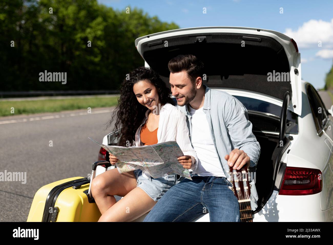 Positive couple going on road trip in car, looking at map, taking break ...