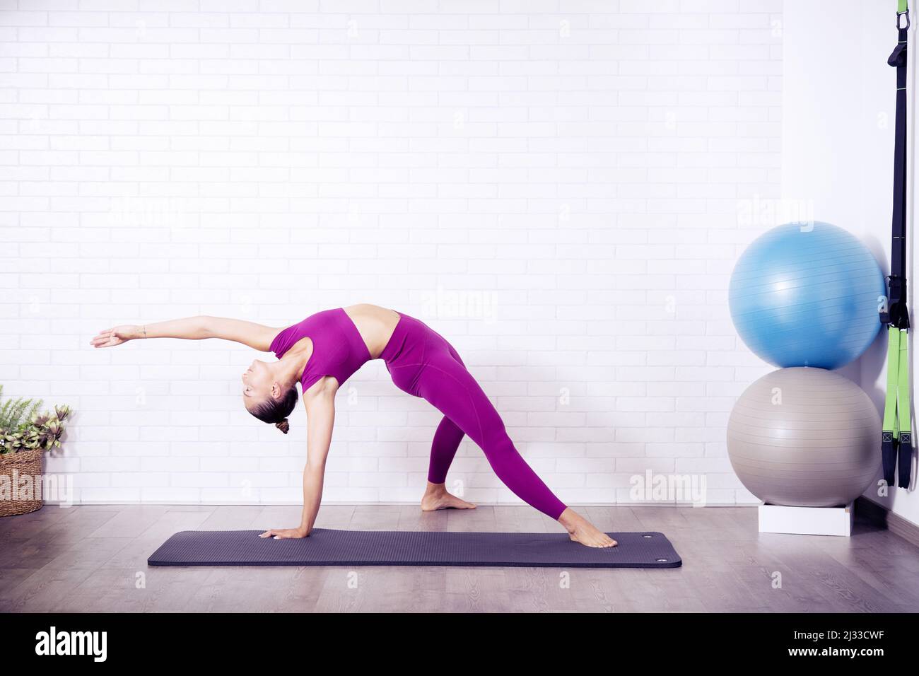 A Caucasian female doing yoga pose on gym studio on a mat in background ...