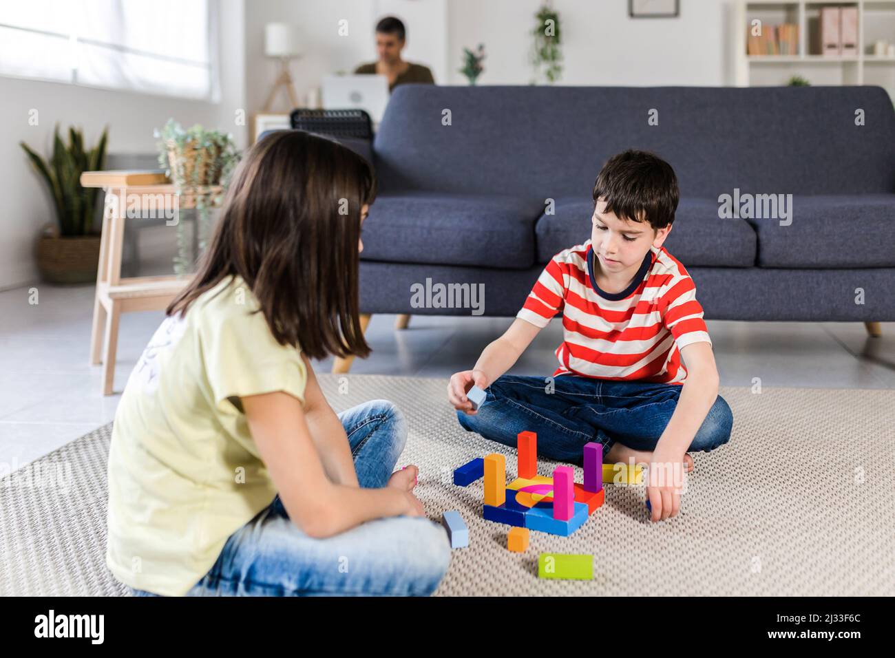 Two kids playing together on the floor while their father working with ...