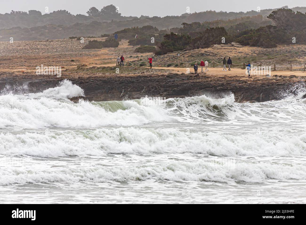 A group of people watching ocean waves against a rocky coast Stock ...