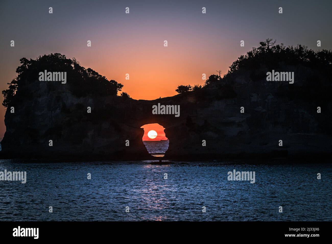 A beautiful view of a sea and cliffs with the sun seen through a cliff ...
