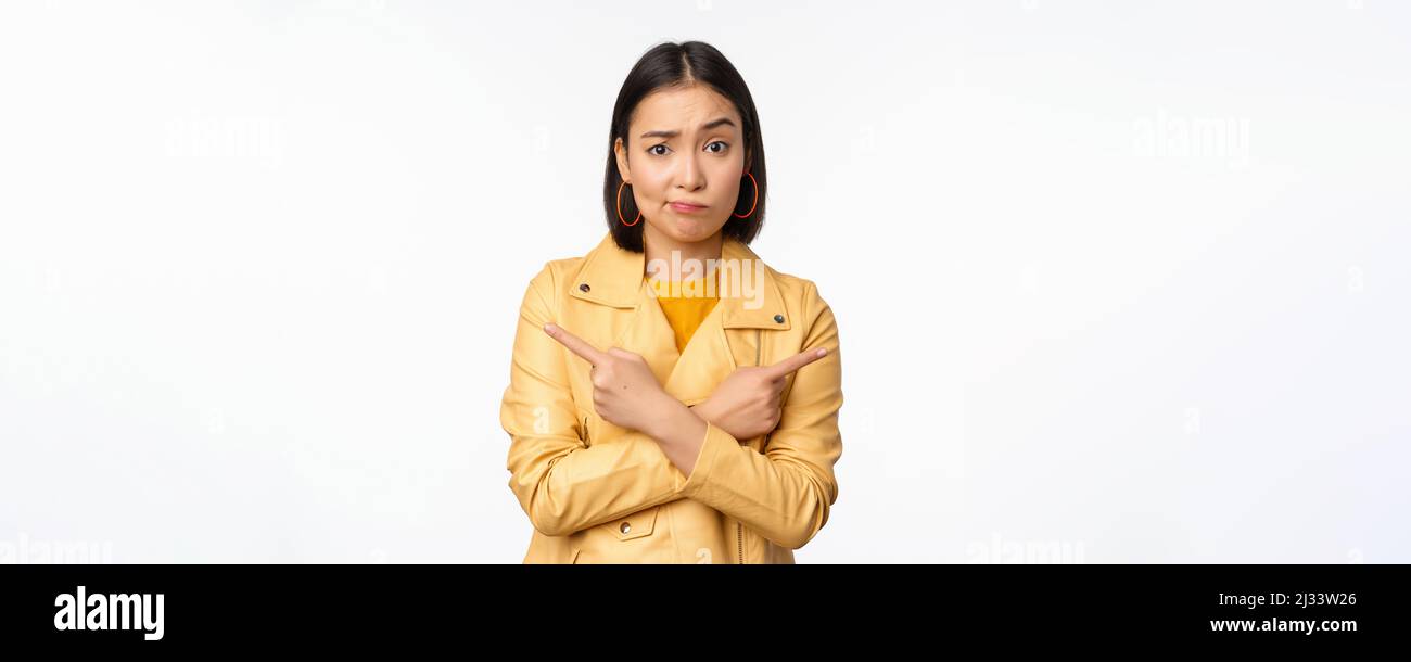 Image of indecisive asian girl, pointing fingers sideways, pointing ...