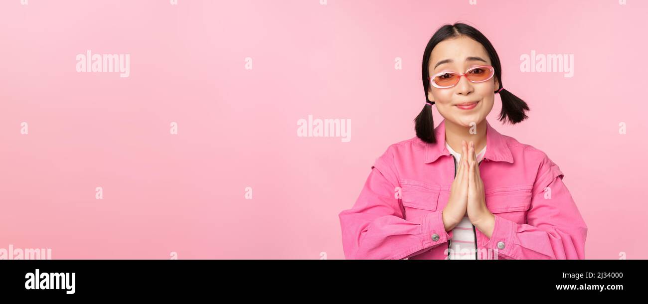 Please. Cute asian girl asking favour, begging, standing against studio ...