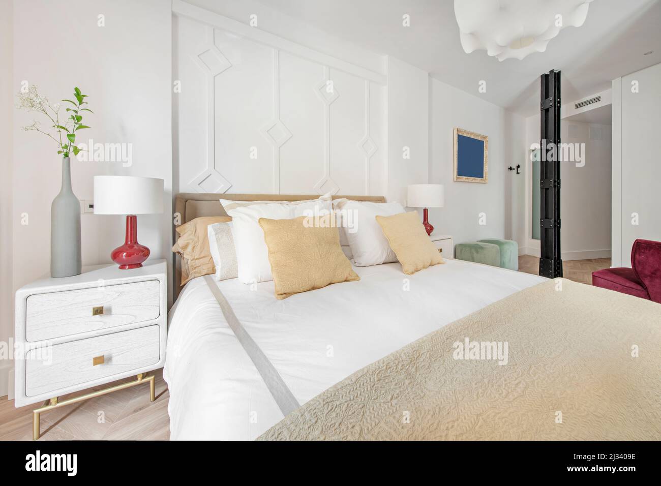 Bedroom with double bed with light colored cushions, light wood bedside ...