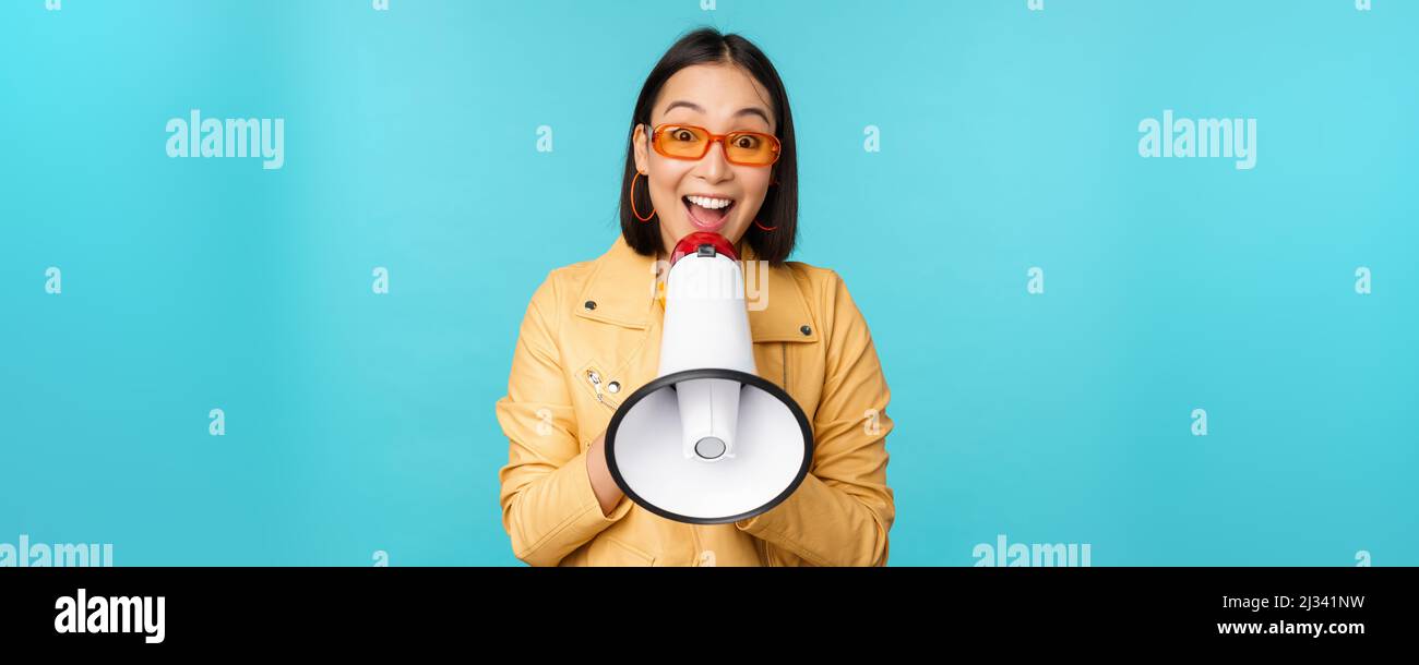 Stylish asian girl making announcement in megaphone, shouting with ...