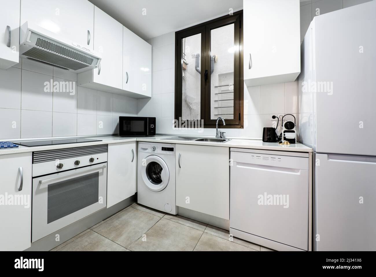 Corner of a fully fitted white kitchen with matching white appliances ...
