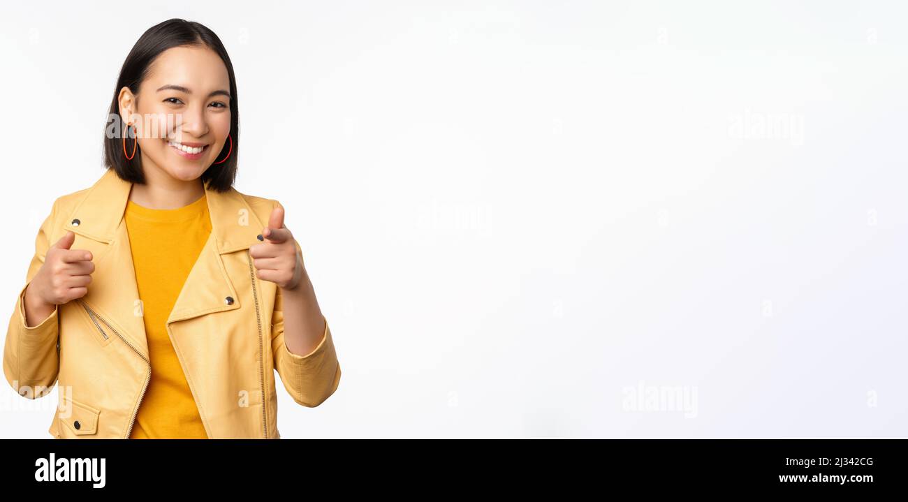 Hey you. Happy smiling asian woman pointing fingers at camera, choosing ...